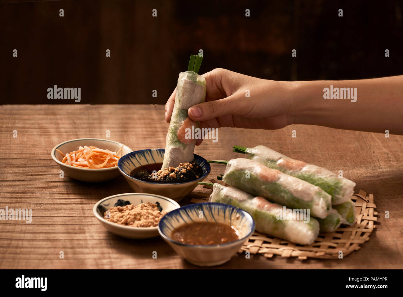 Young woman's hands eating healthy spring roll dipped in a soya sauce ...