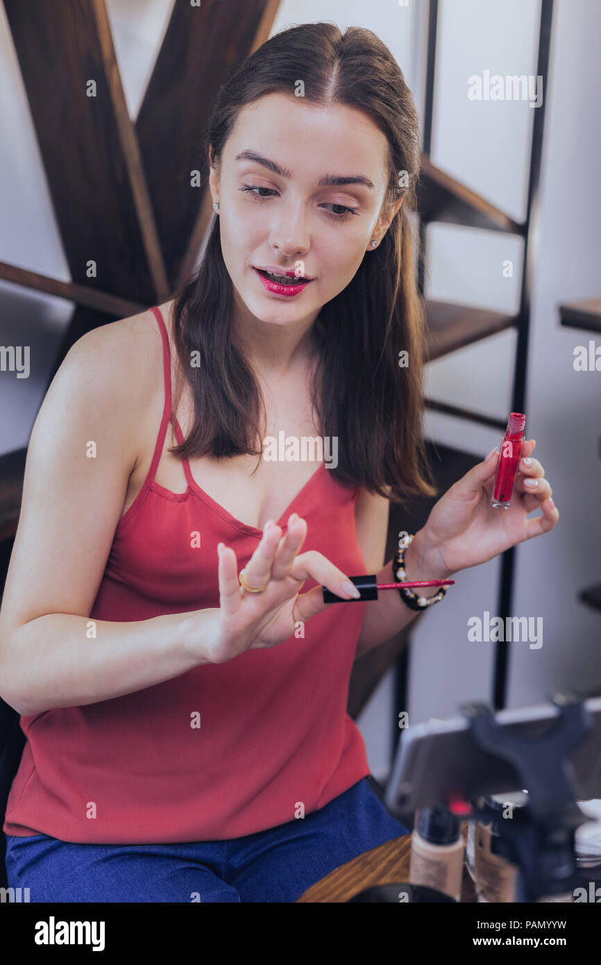 Beautiful blogger wearing jeans and red blouse telling about lip gloss ...