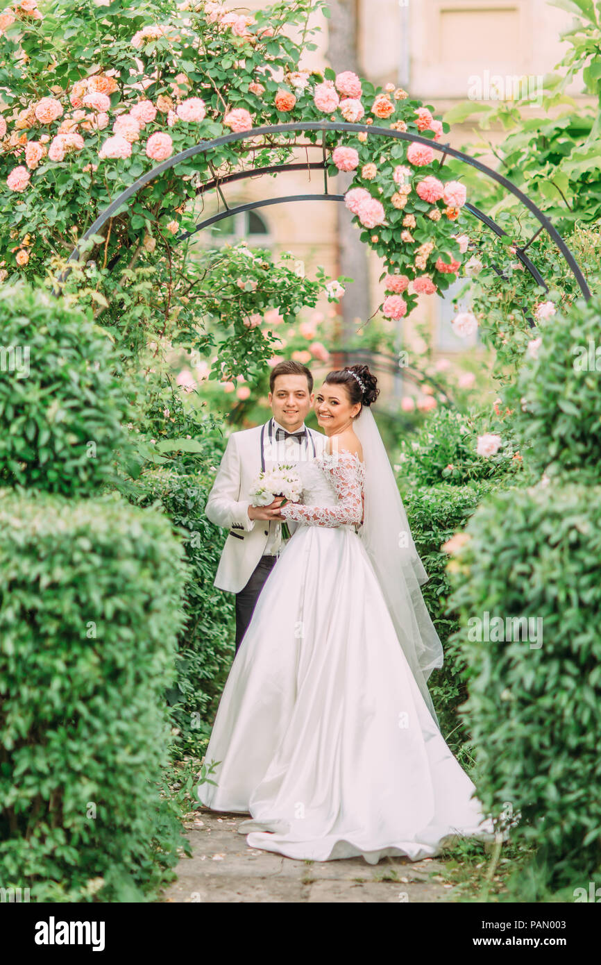 Full-length photo of the hugging newlyweds under the roses arch Stock ...
