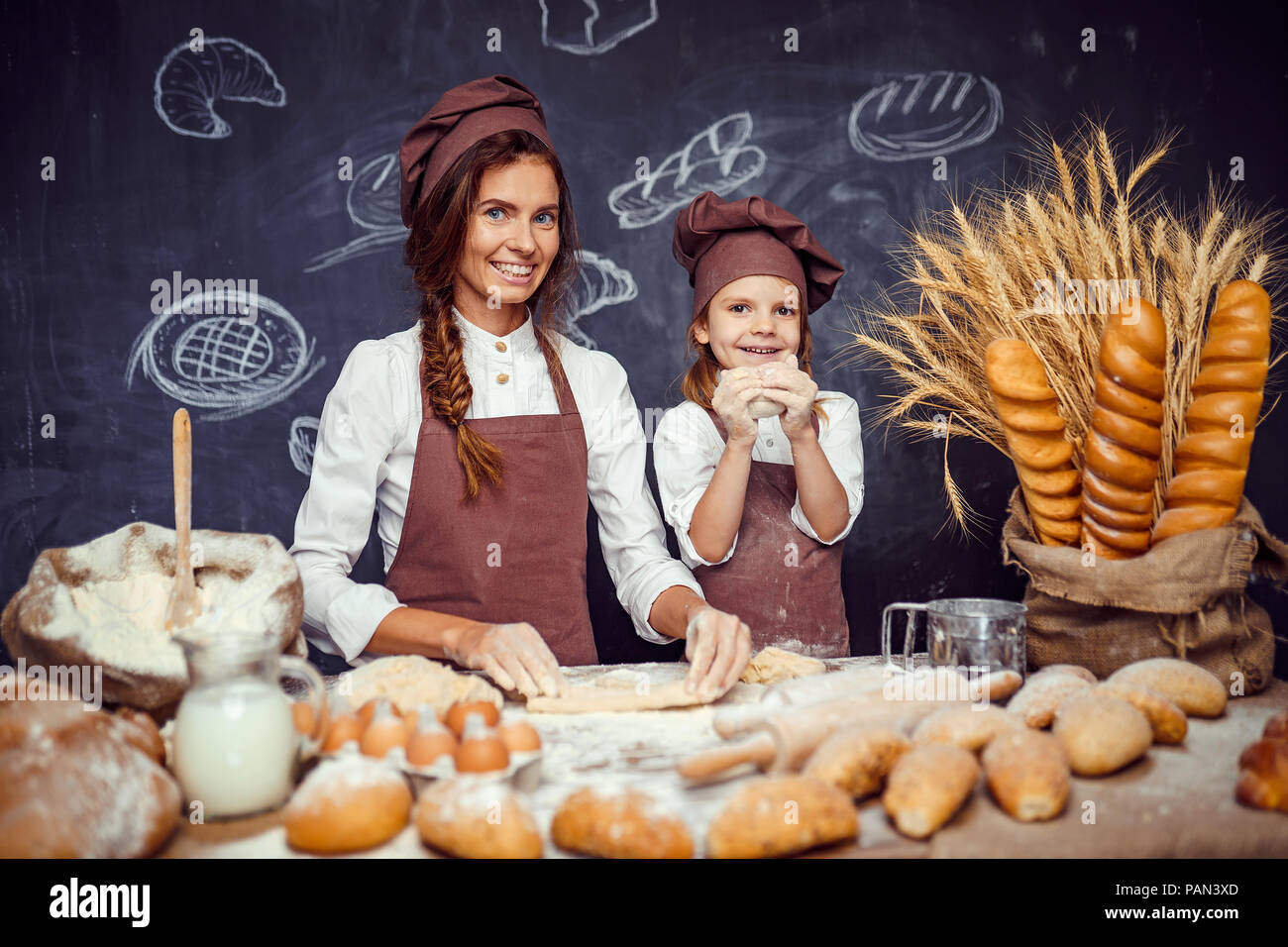 Woman with little girl in hats and aprons making pastries from dough ...