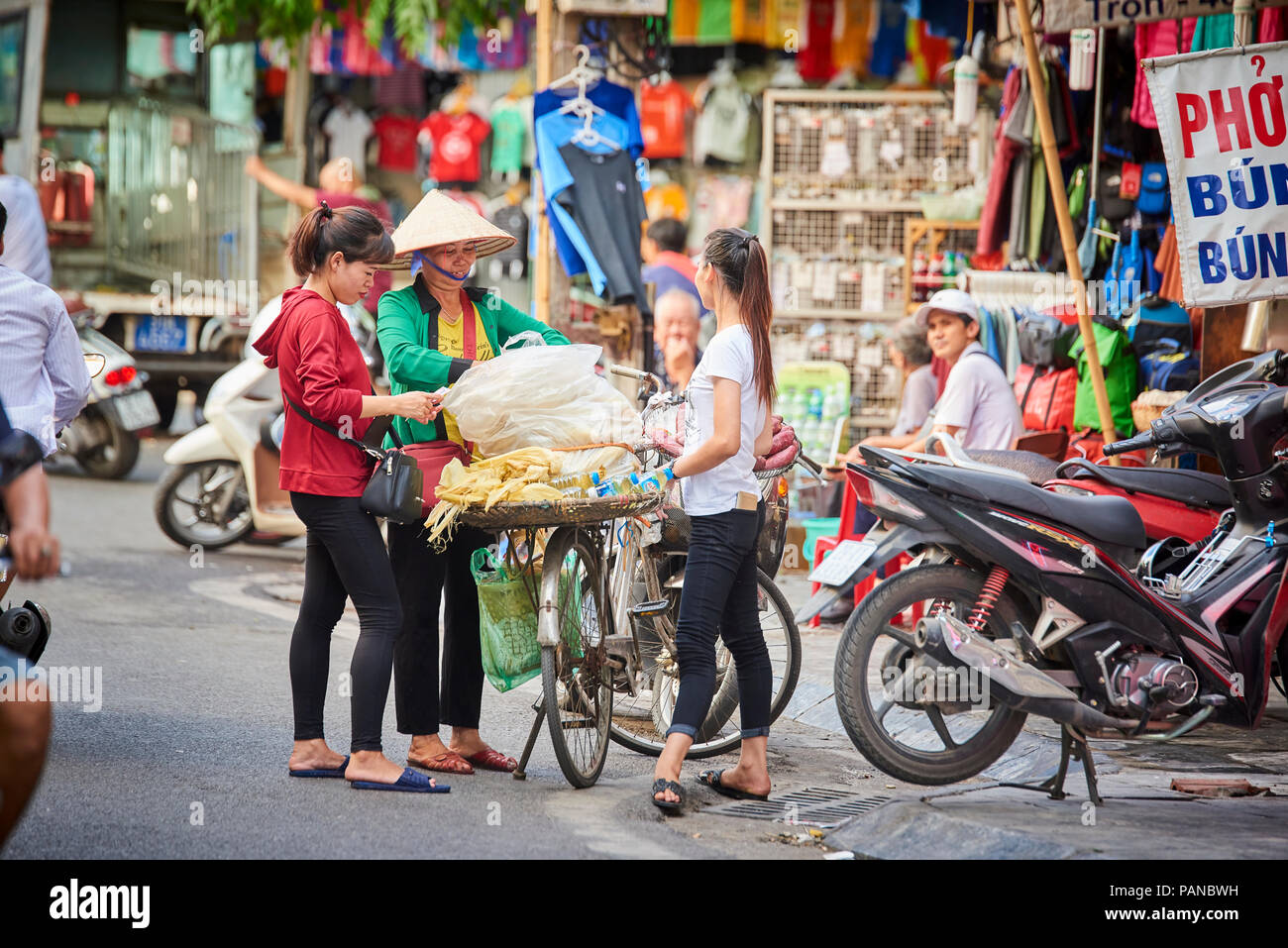 A street seller wearing traditional conical straw hat helping customers ...