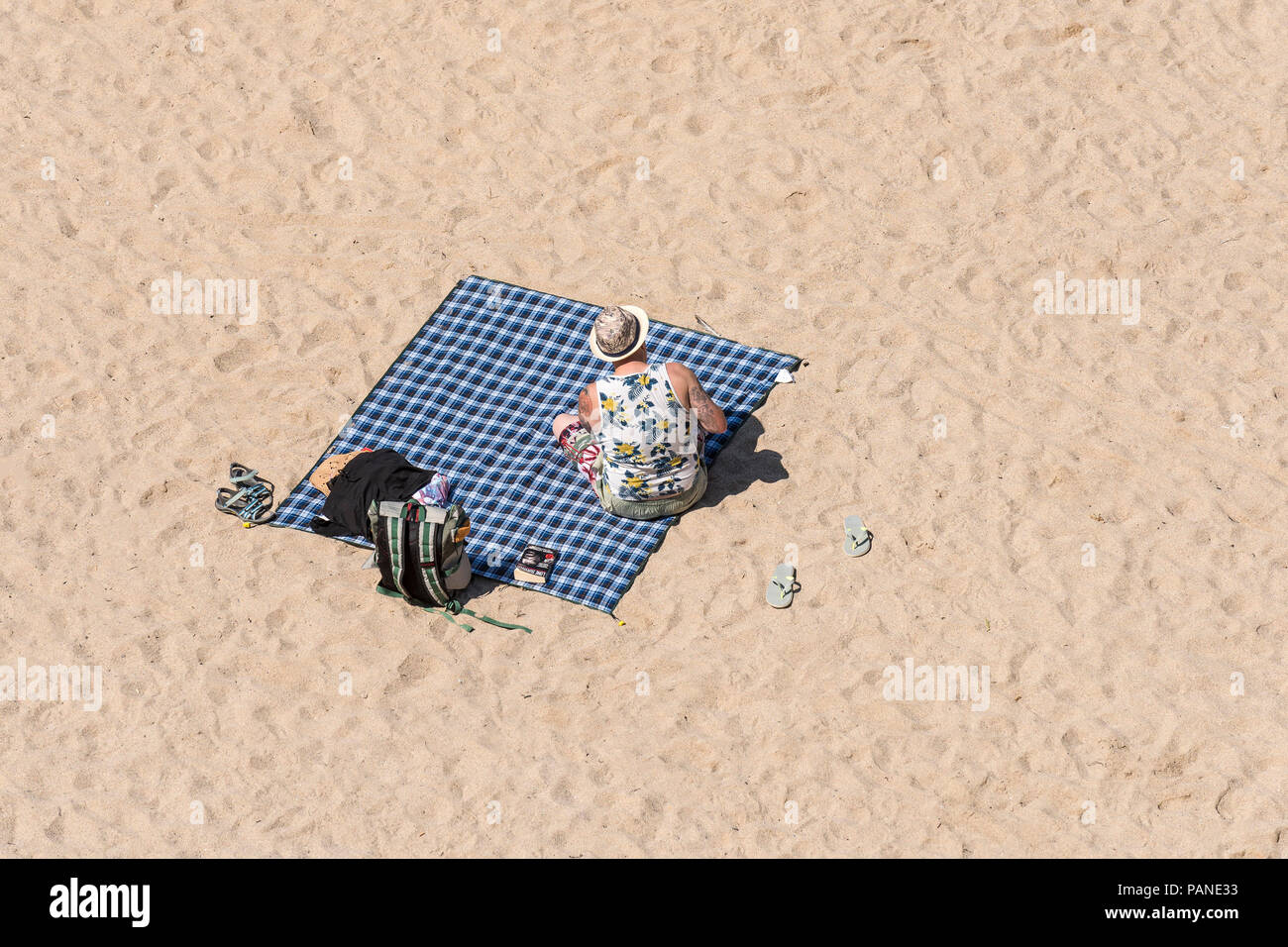 A holidaymaker person sitting on a beach in Newquay in Cornwall Stock ...