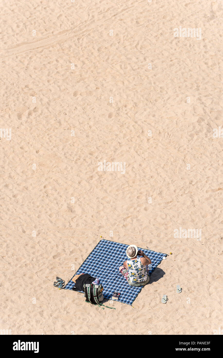 A holidaymaker person sitting on a beach in Newquay in Cornwall Stock ...