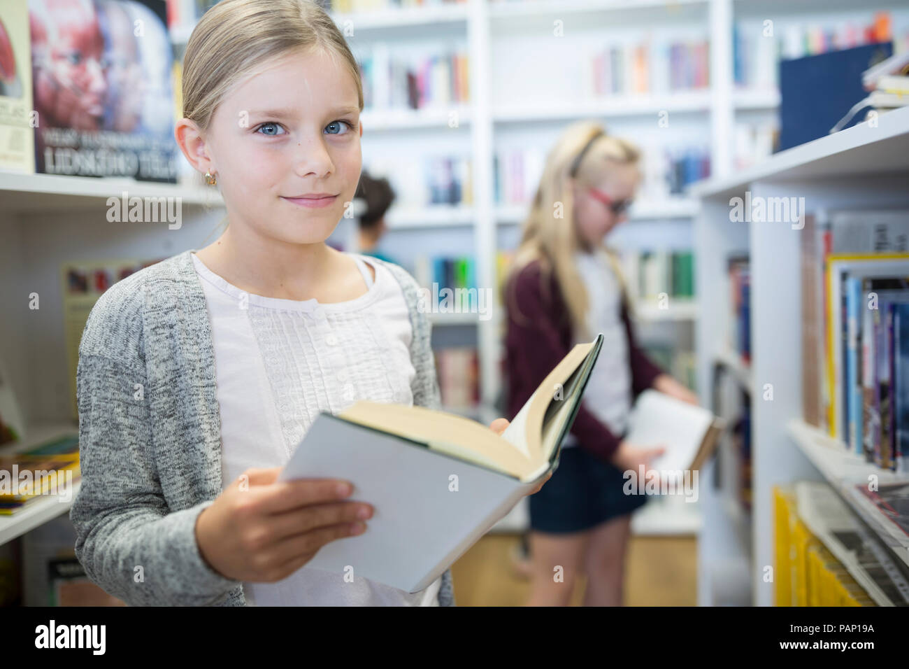 Portrait of smiling schoolgirl with book in school library Stock Photo ...