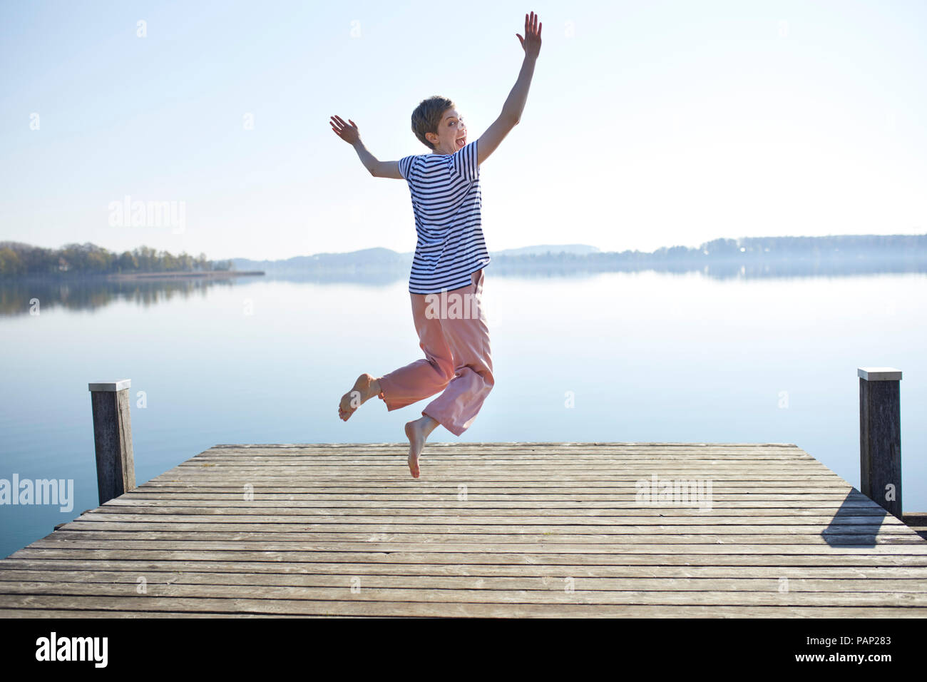 Germany, Bavaria, back view of woman jumping in the air in front of ...