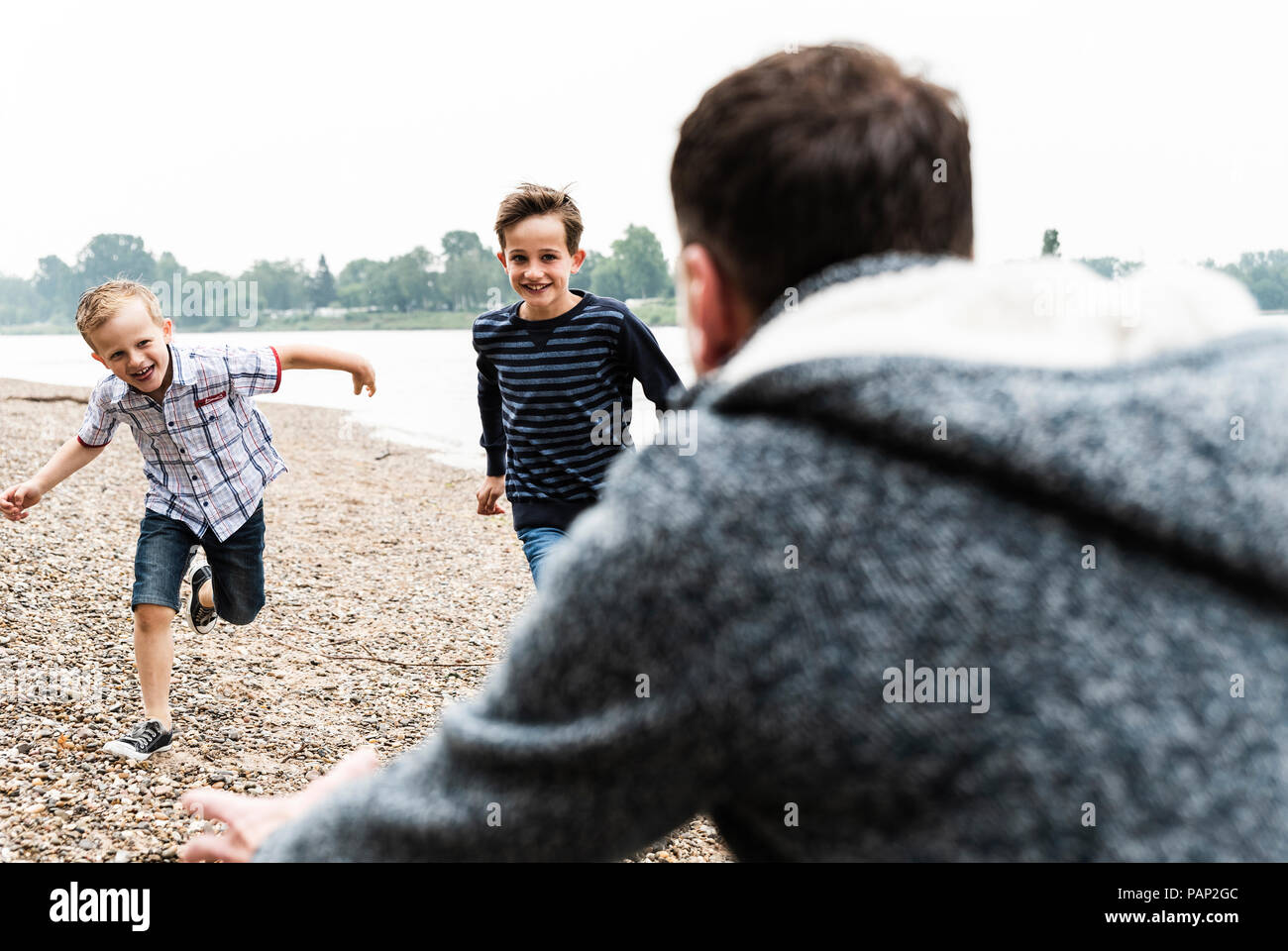 Happy boys running towards father at the riverside Stock Photo - Alamy