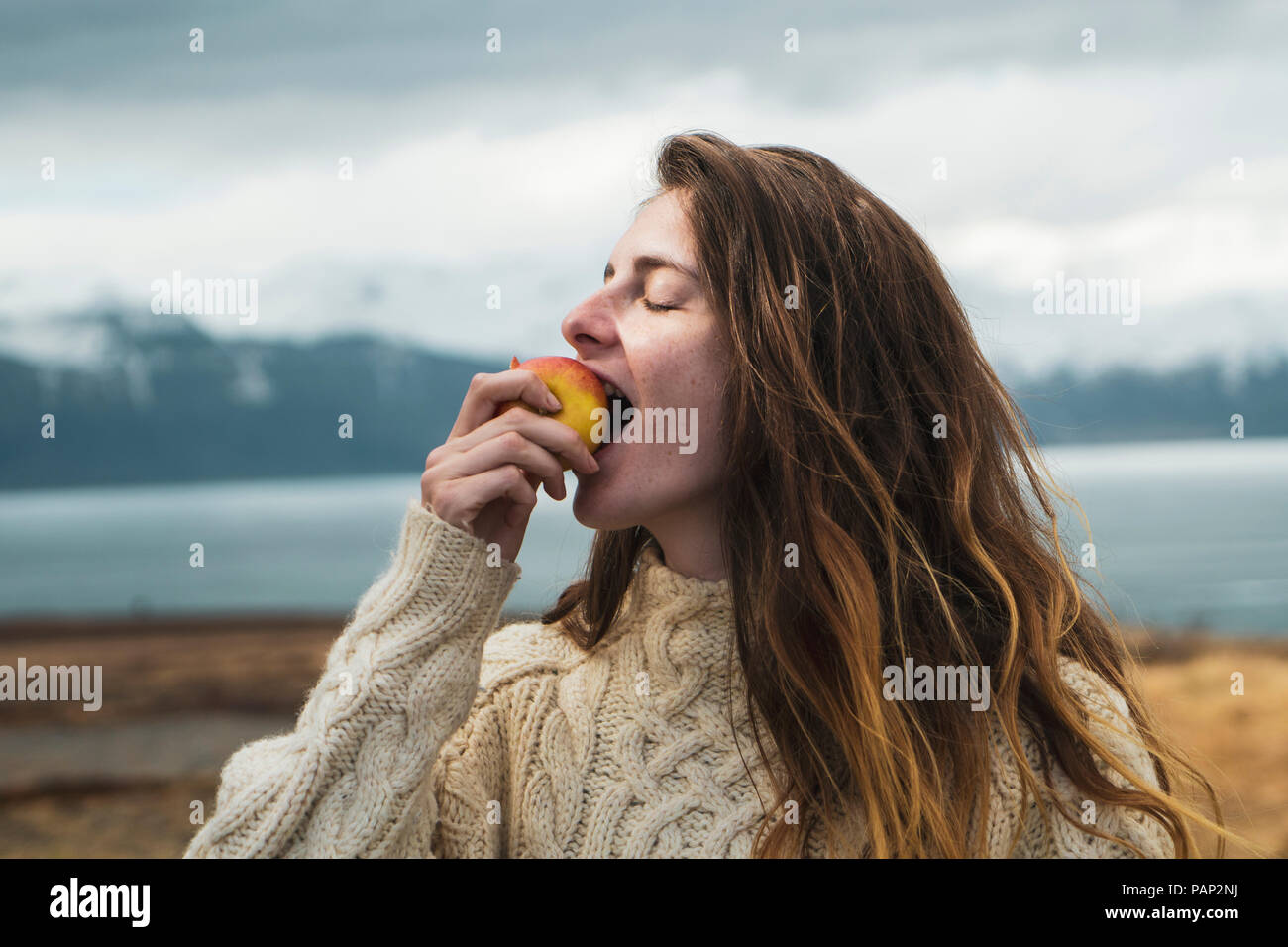 Iceland, woman eating an apple at lakeside Stock Photo - Alamy