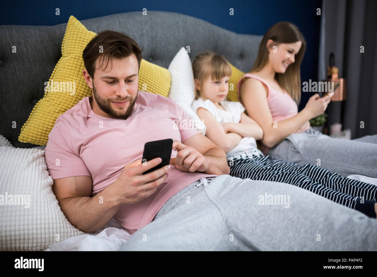 Neglected little girl sitting on bed with her parents, using ...