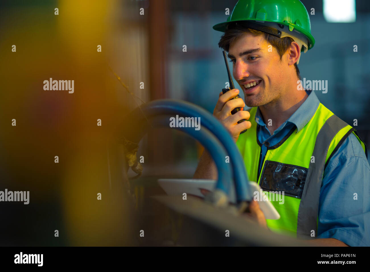 Engineer in industrial plant inspecting machines, using walkie-talkie ...