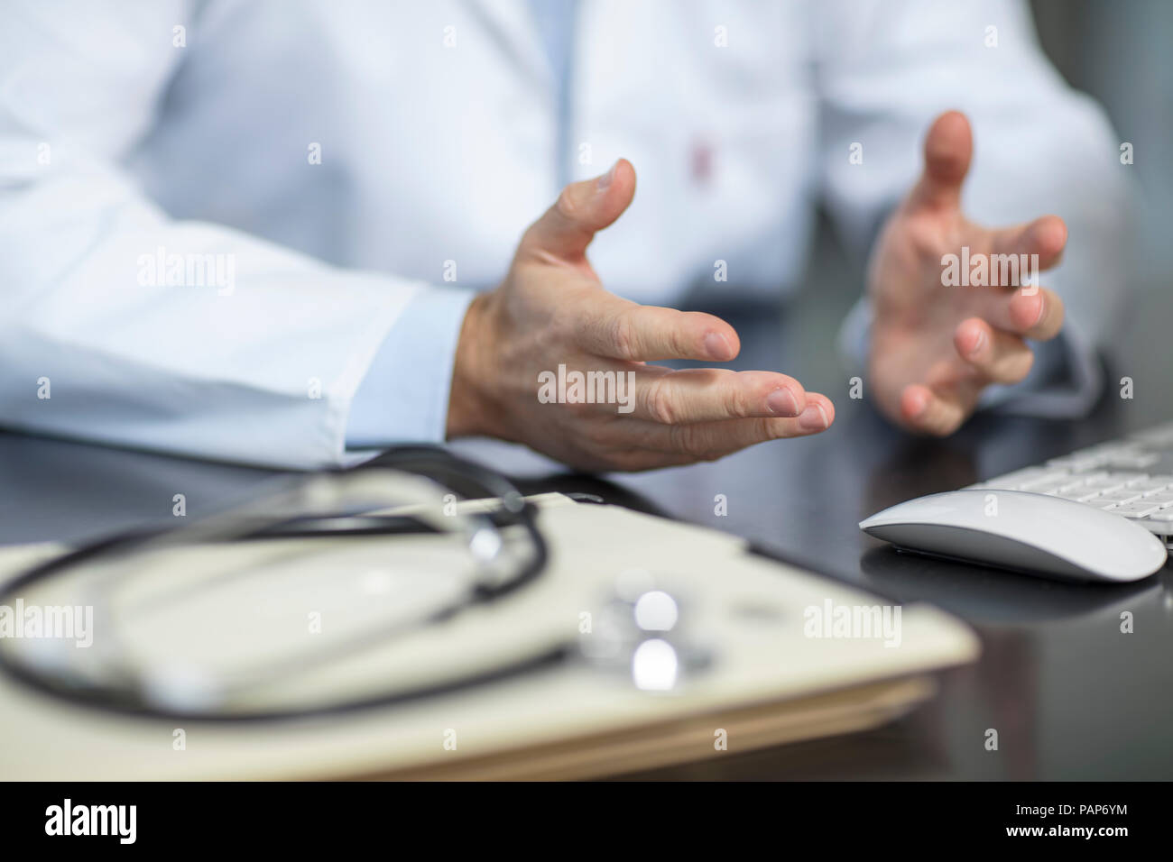 Files and stethoscope on desk in medical practice with doctor gesturing ...