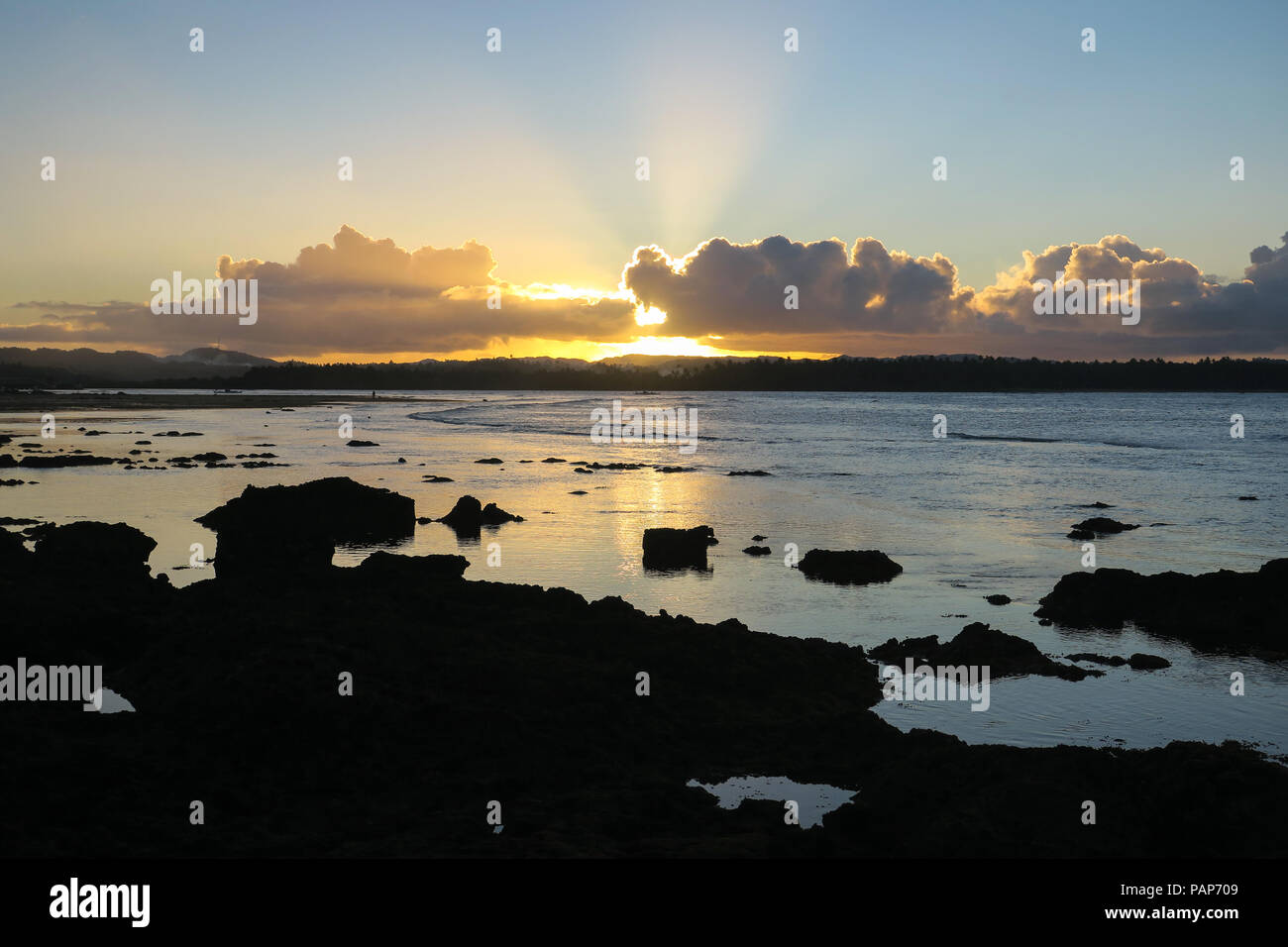 Golden clouds and light from sun rays during rocky island beach sunset ...