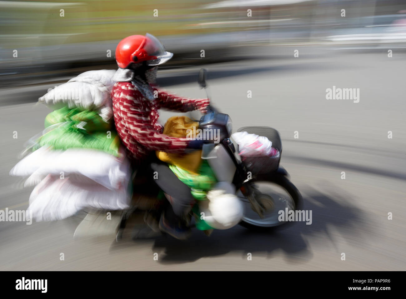 Panning photo of motion blurred moped rider carrying bags in the ...