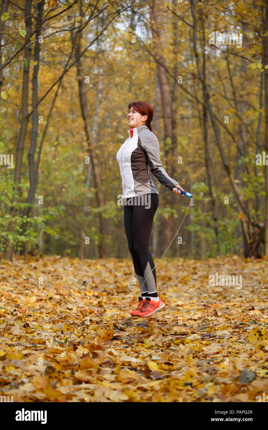 Full-length picture of athlete girl jumping with rope at autumn forest ...