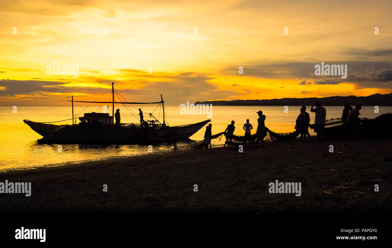 Group of Filipino Fishermen dragging a net from a boat to the beach ...
