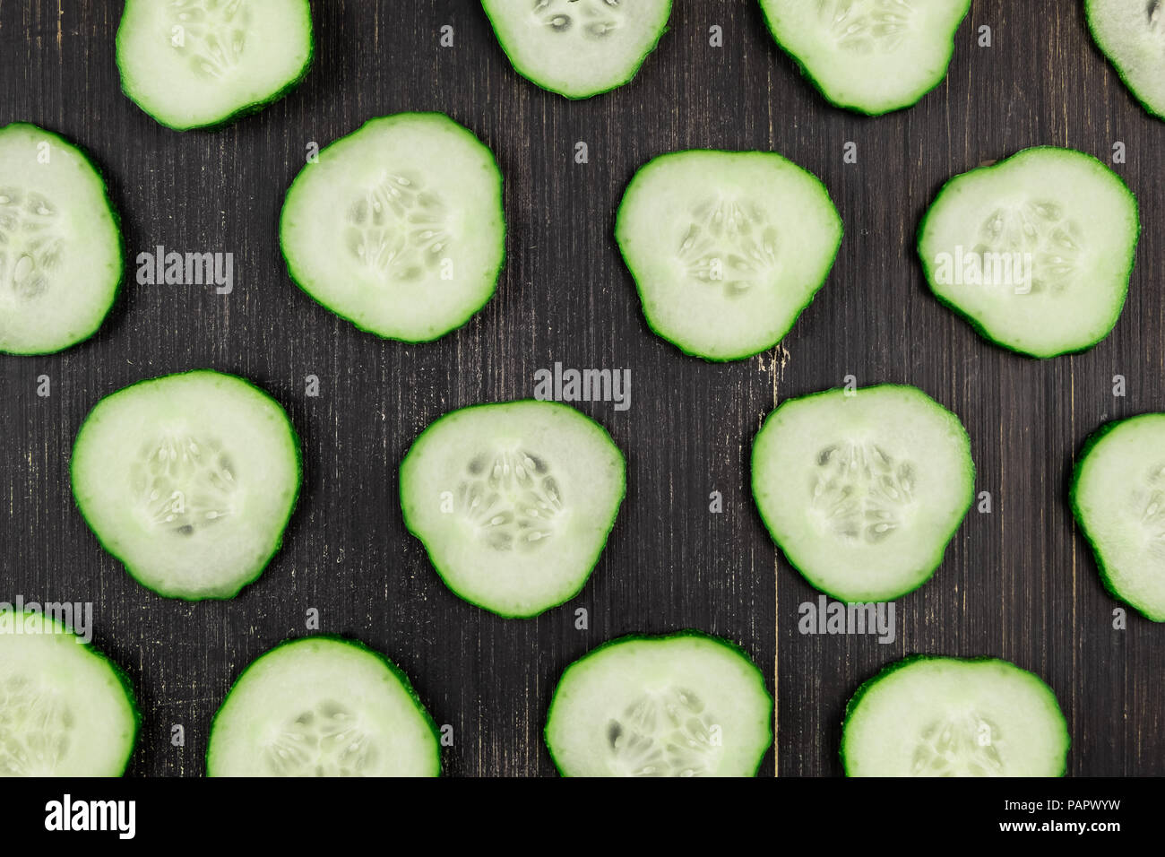 Fresh sliced cucumbers on black wood rustic background, top view. Flat ...