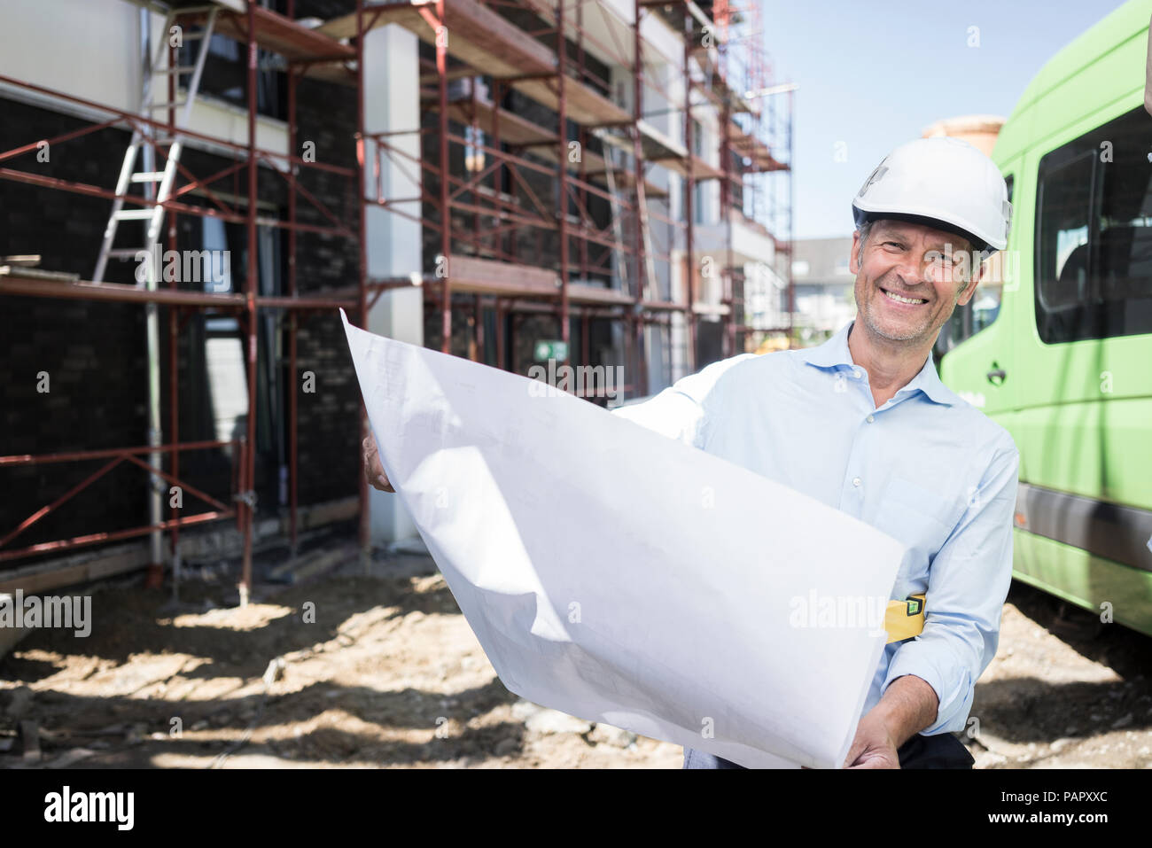 Portrait of smiling architect with blueprint wearing hard hat on ...