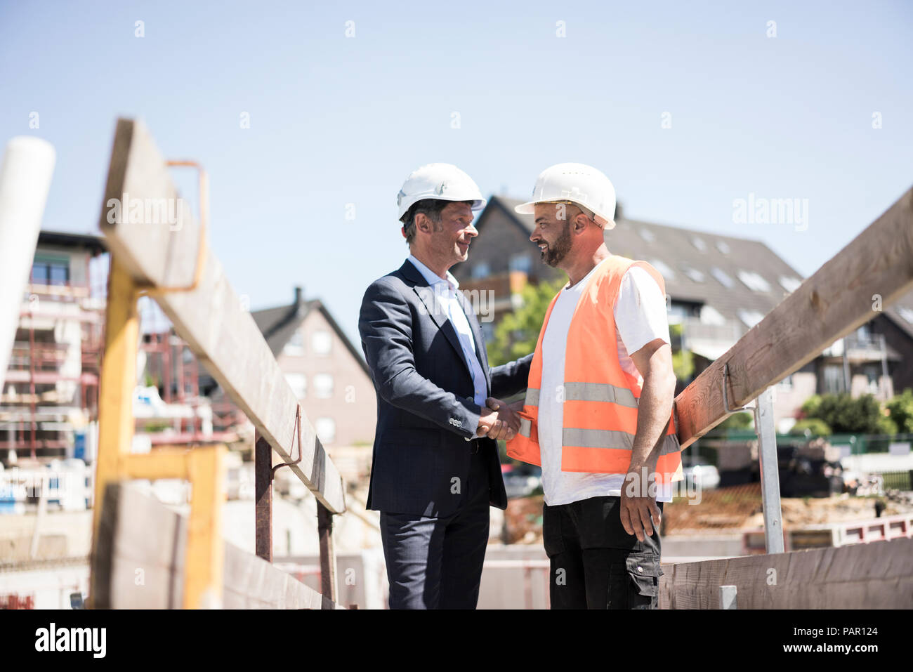 Man in suit shaking hands with construction worker on construction site ...