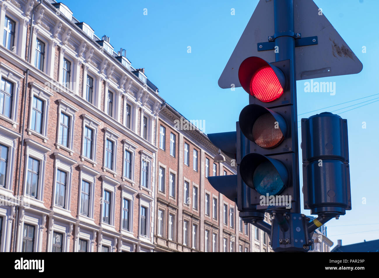 A traffic stop light is on red with typical Danish buildings in the ...