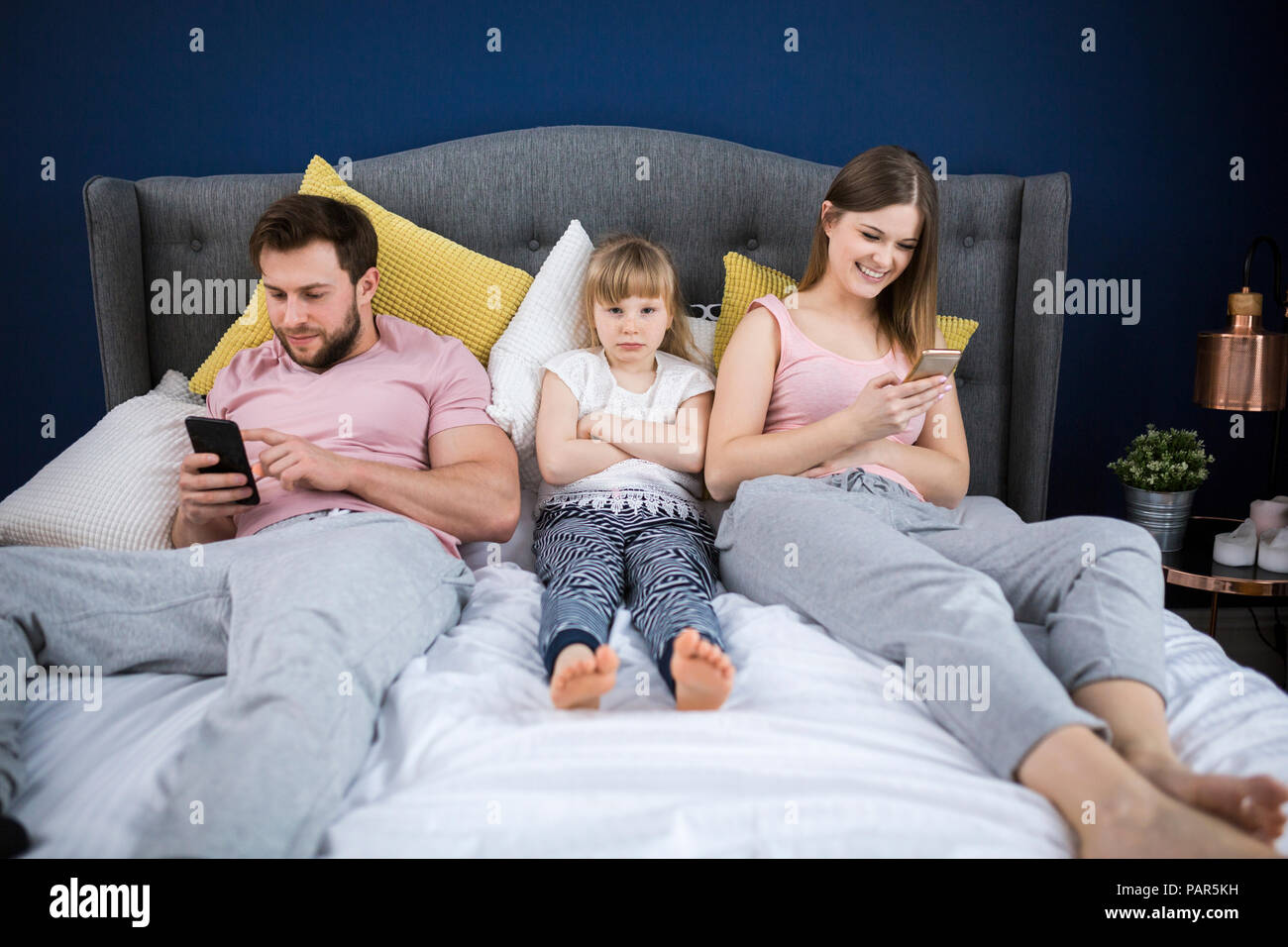 Neglected little girl sitting on bed with her parents, using ...