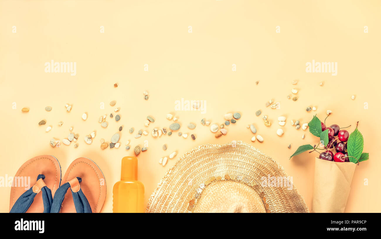 Top view of flip flops, straw hat and cherries on yellow background ...