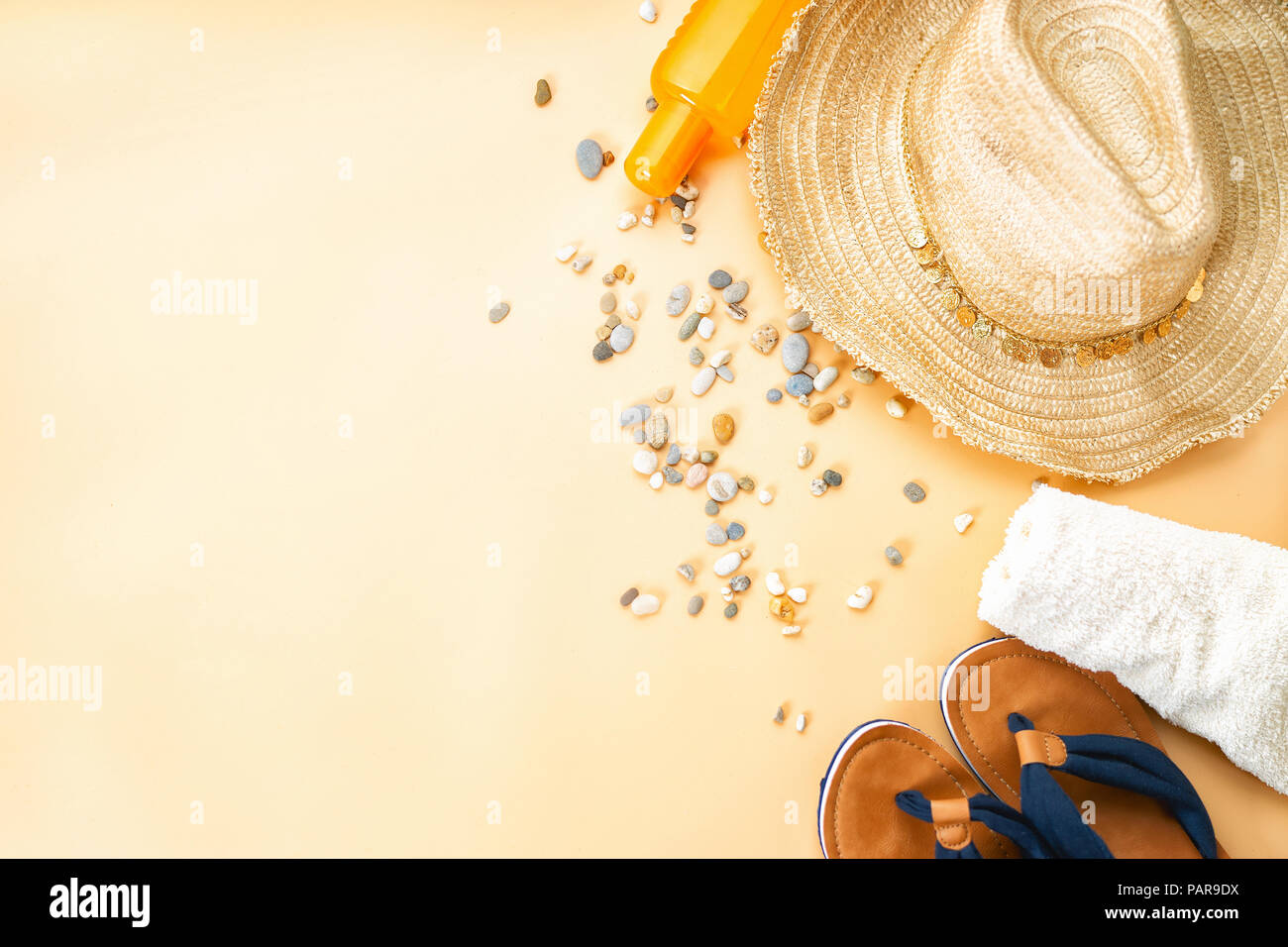 Top view of flip flops, straw hat and white towel on yellow backkground ...