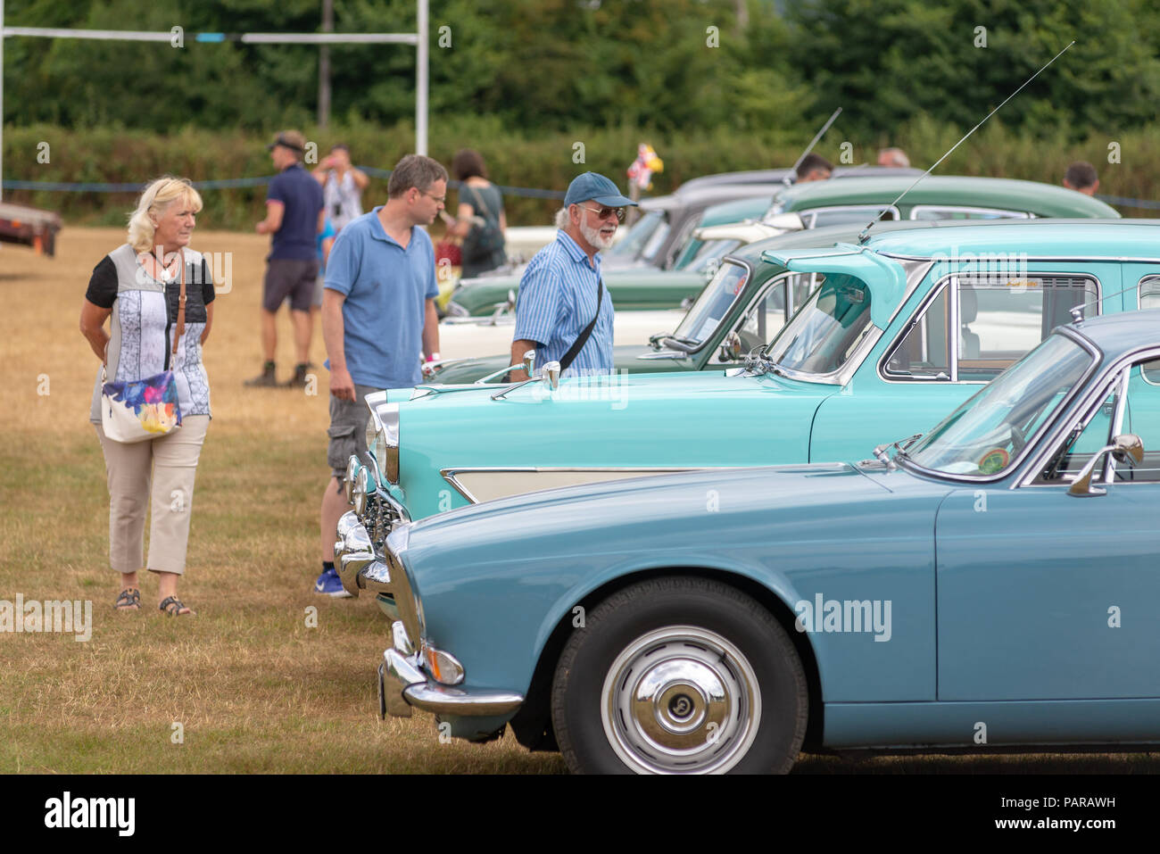 People looking at vintage cars parked in a row at a country fair in ...