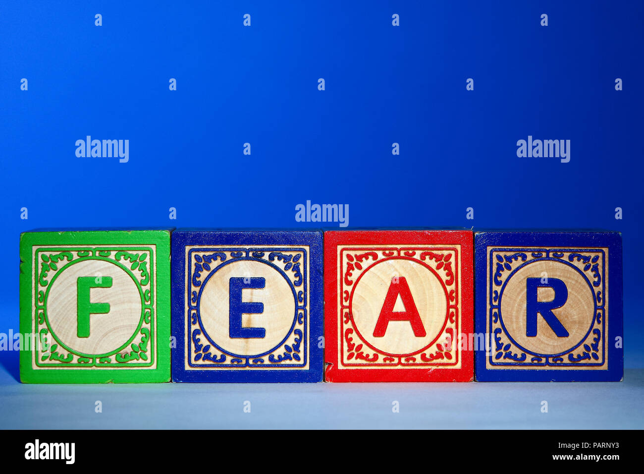 Wooden letter blocks on a blue background spelling out the word fear ...