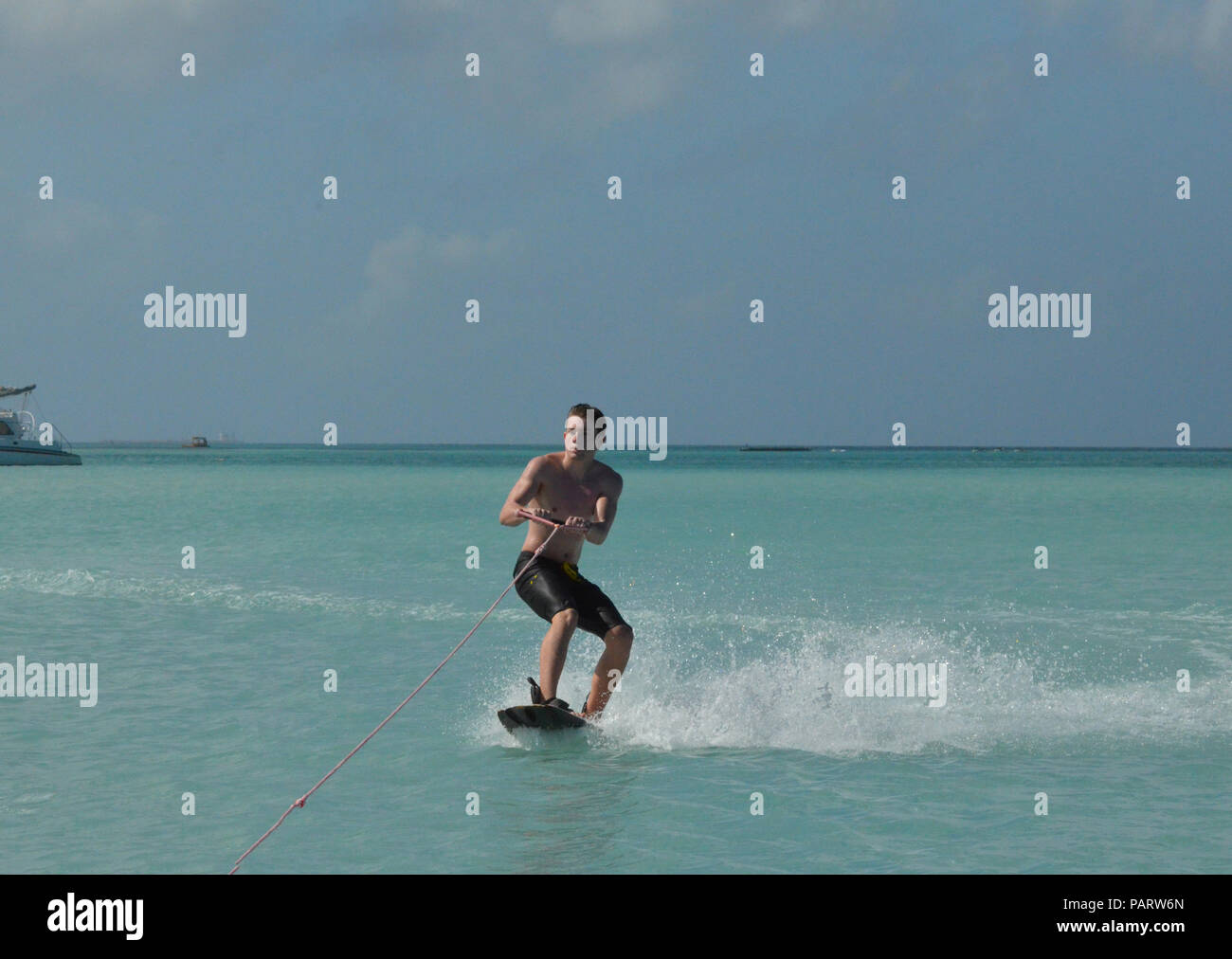 Young guy crouching while wakeboarding in Aruba Stock Photo - Alamy