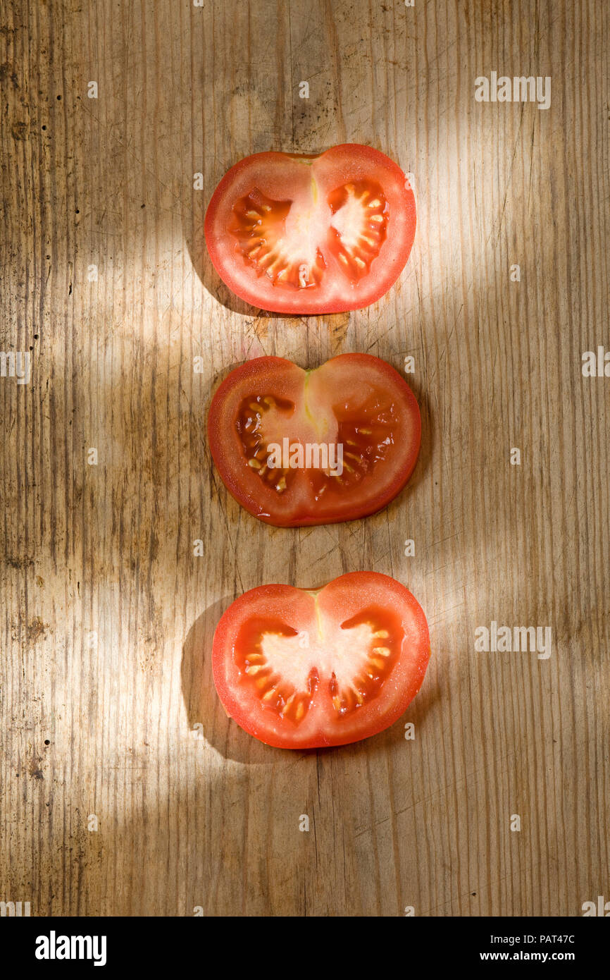 Three sliced red tomatoes on wood background Stock Photo - Alamy