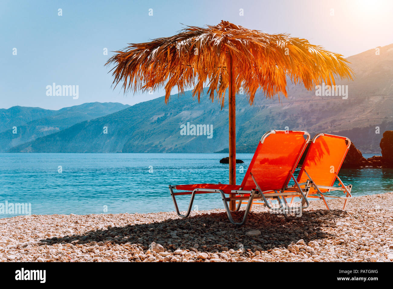 Lovely isolated beach and sunbeds under straw umbrella at warm sunset ...