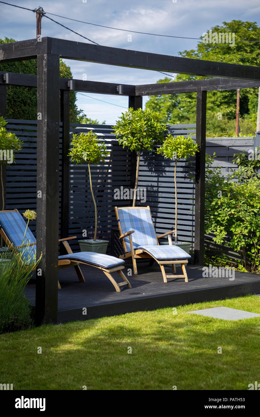 Cube pergola seating area painted black, with deck chairs and topiary ...