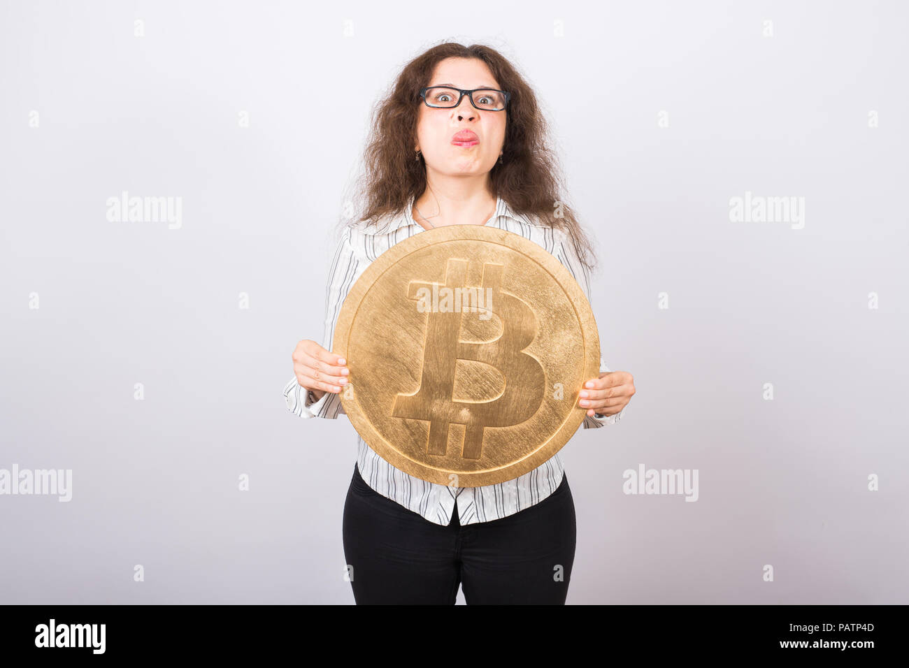 Angry young woman holding big golden bitcoin and showing tongue ...