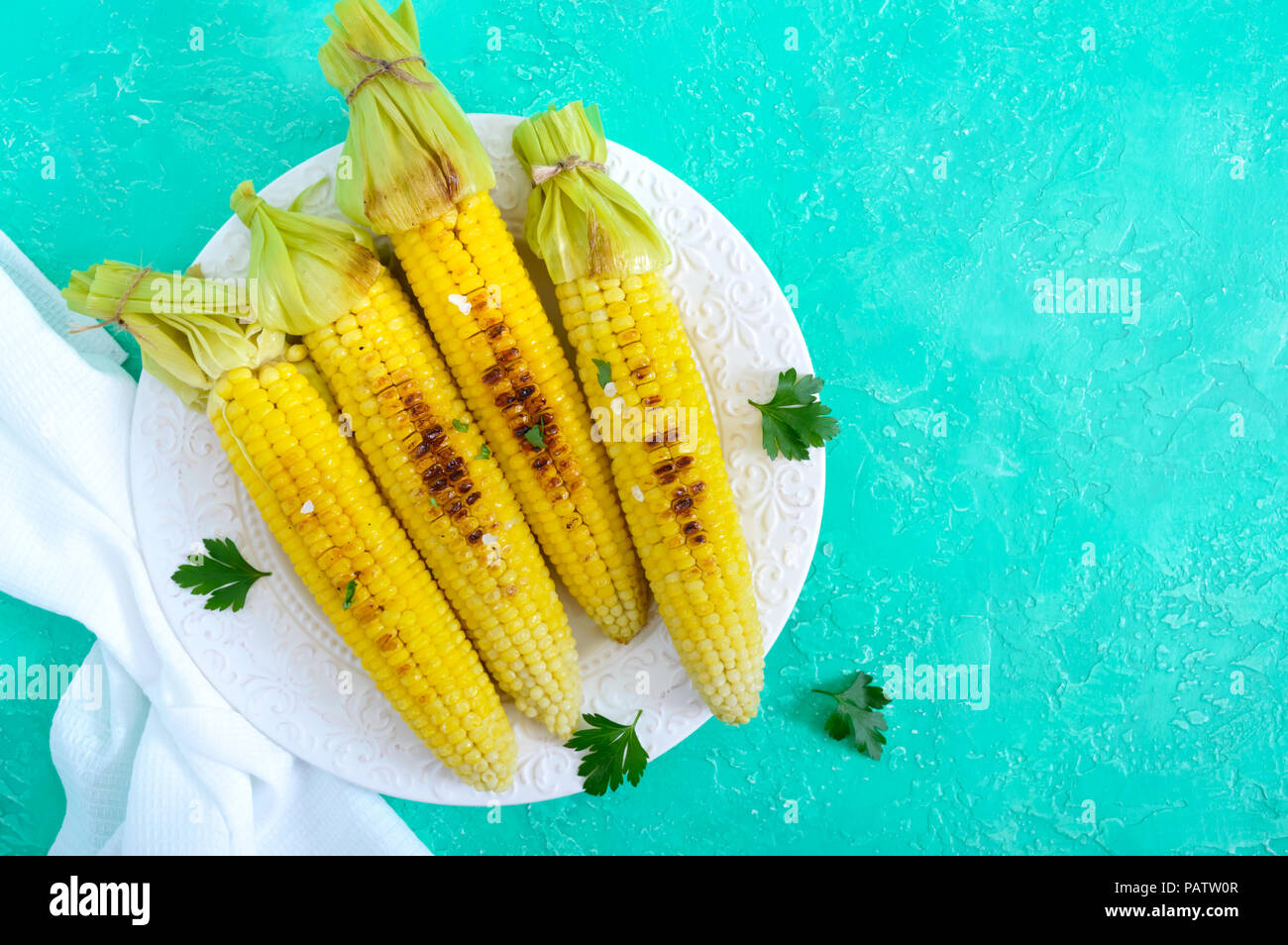 Grilled corn with herbs and sea salt on a white plate on a bright ...