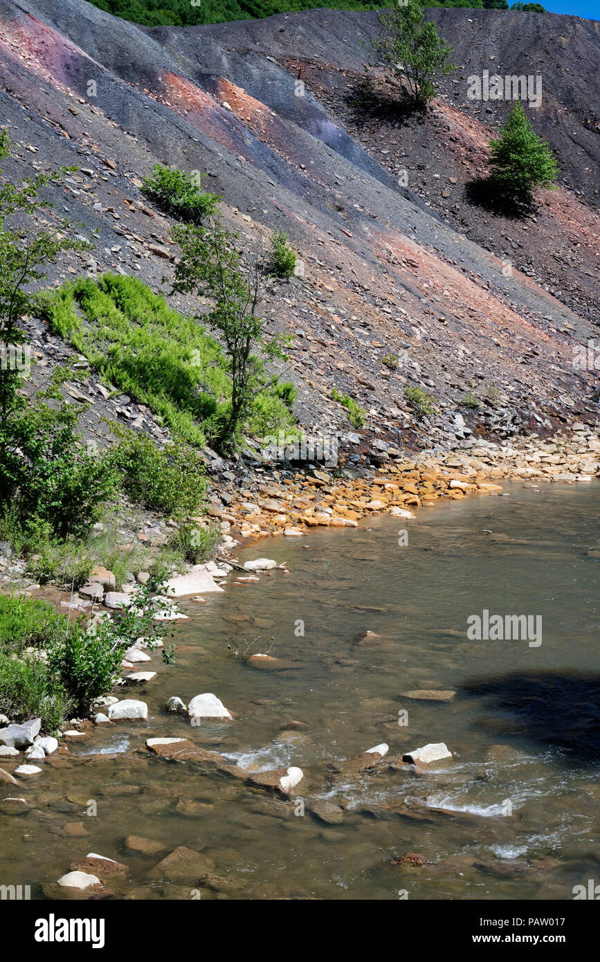 Coal mine tailings waste spoil pile beside a stream with orange rocks ...
