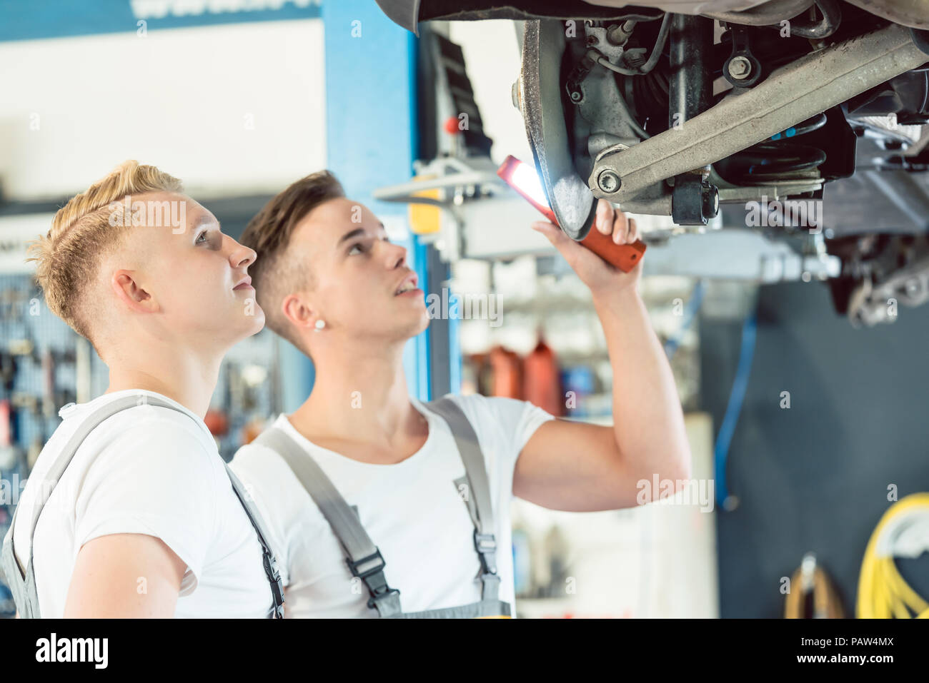 Experienced auto mechanic teaching an apprentice about disk brakes ...