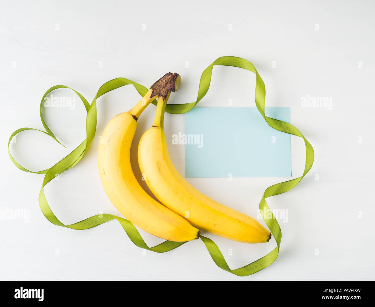 Two bananas with green ribbon frame and heart symbol on white ...