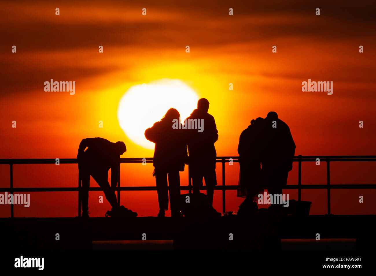 Silhouetted people along a railed walkway as the setting sun glows ...