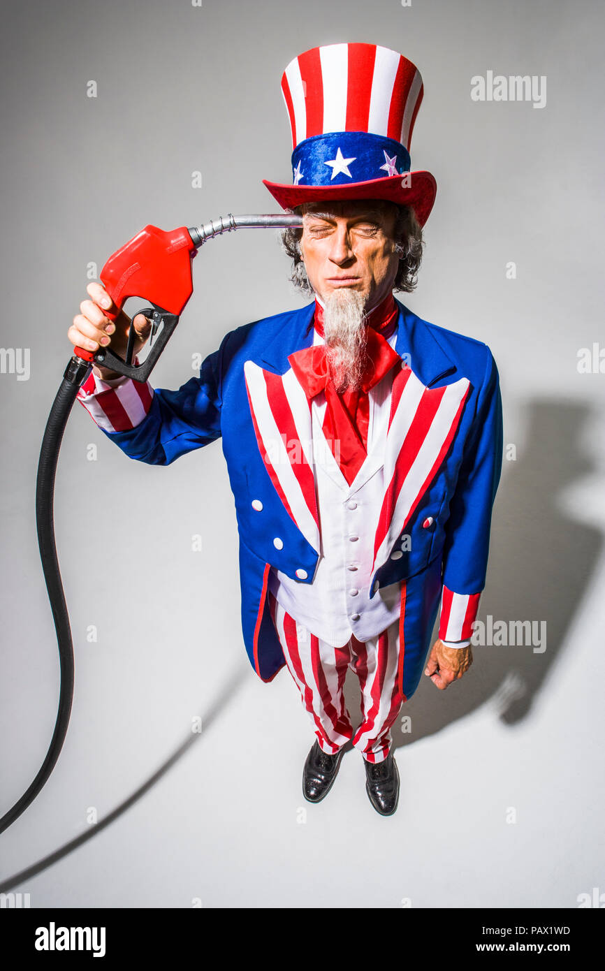 Uncle Sam standing with a gas pump nozzel held in front of him. Conceptual shot depicting the ...