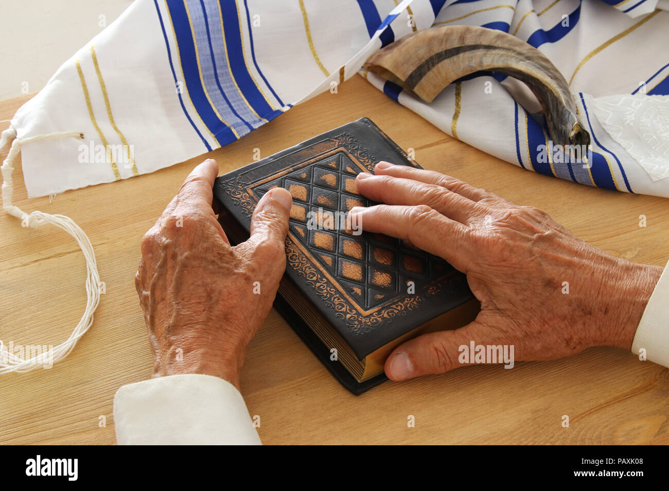 Old Jewish man hands holding a Prayer book, praying, next to tallit and ...