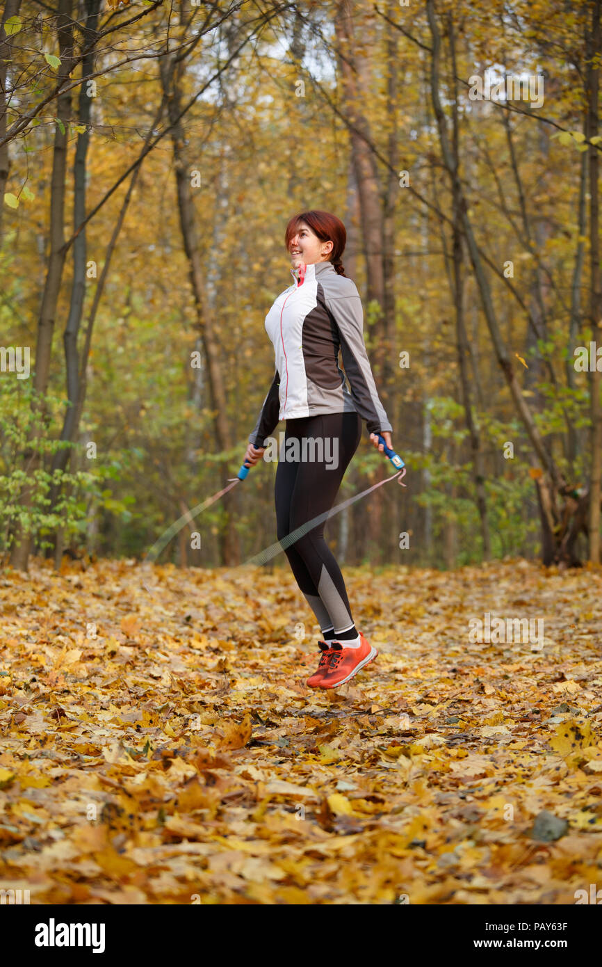 Full-length picture of female athlete jumping with rope at autumn ...