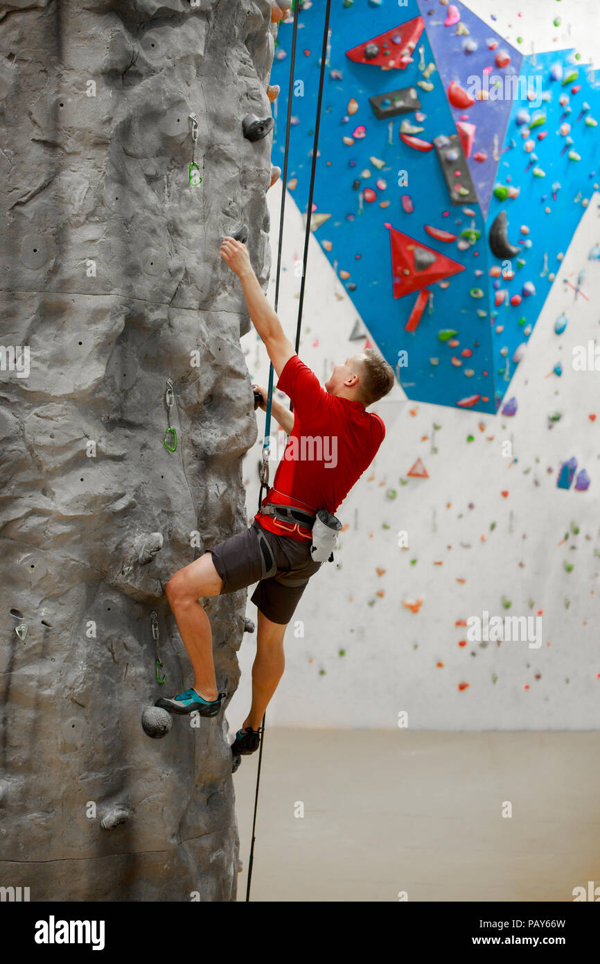 Photo from back of sports male exercising on climbing wall indoors ...