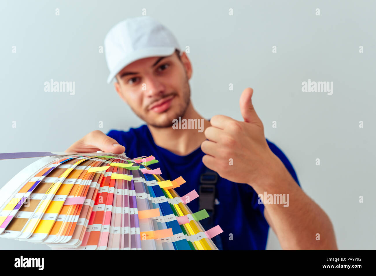 Young worker with thumbs up is holding color guide for wall Stock Photo ...