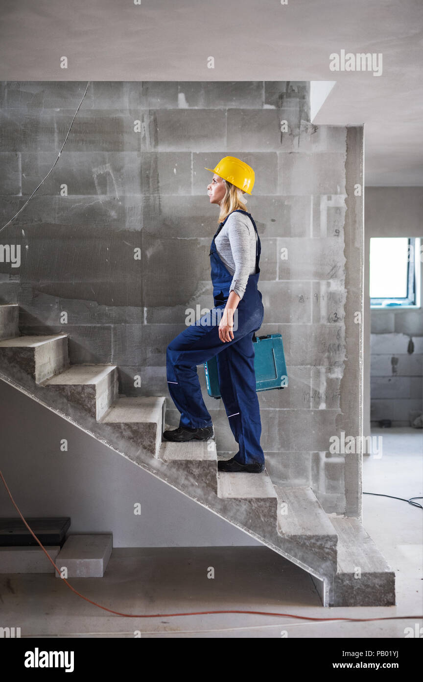 Woman worker with a tool box walking up the stairs on the construction ...