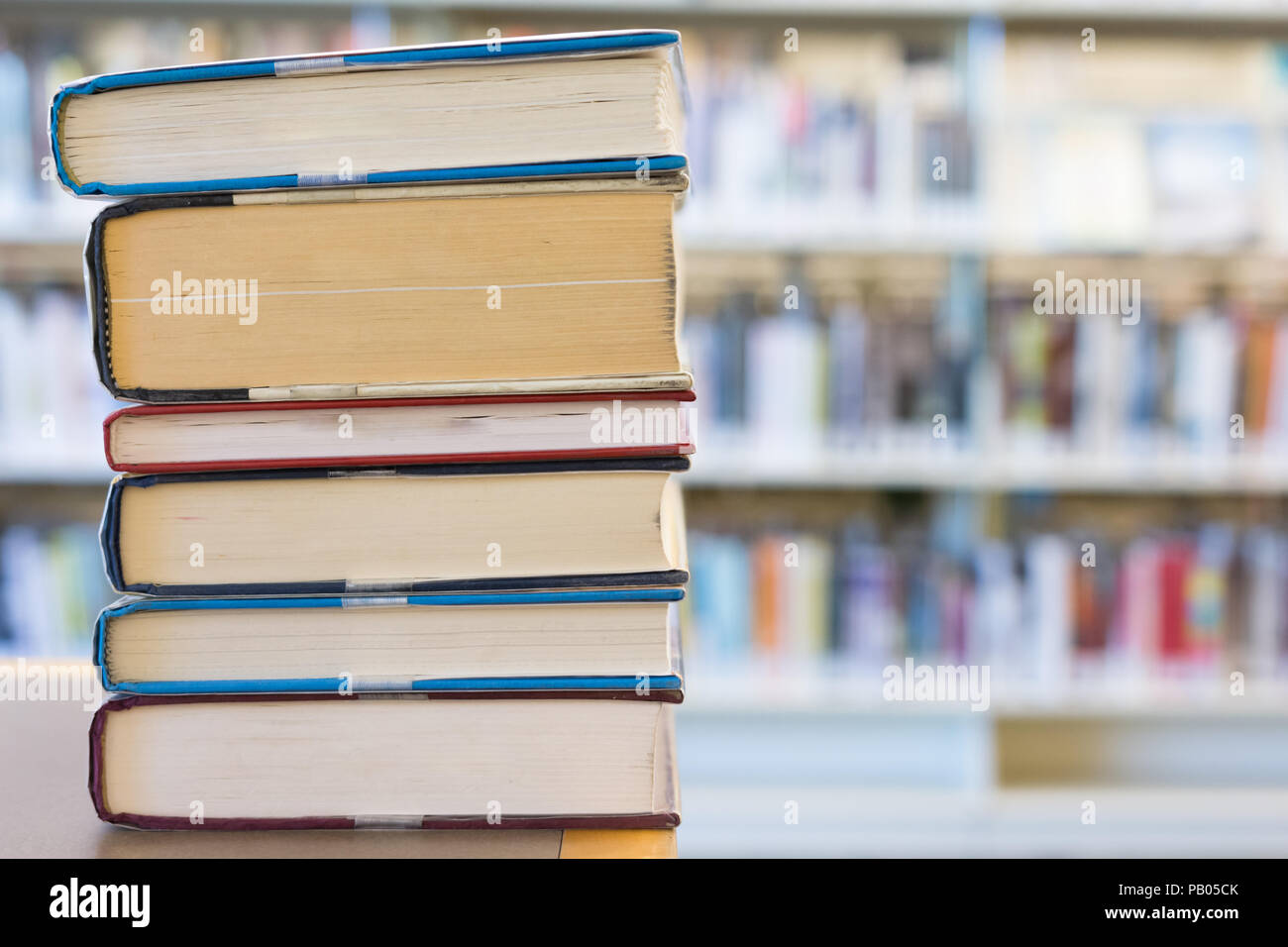 Small stack of various sized books on library desk with shelves of ...
