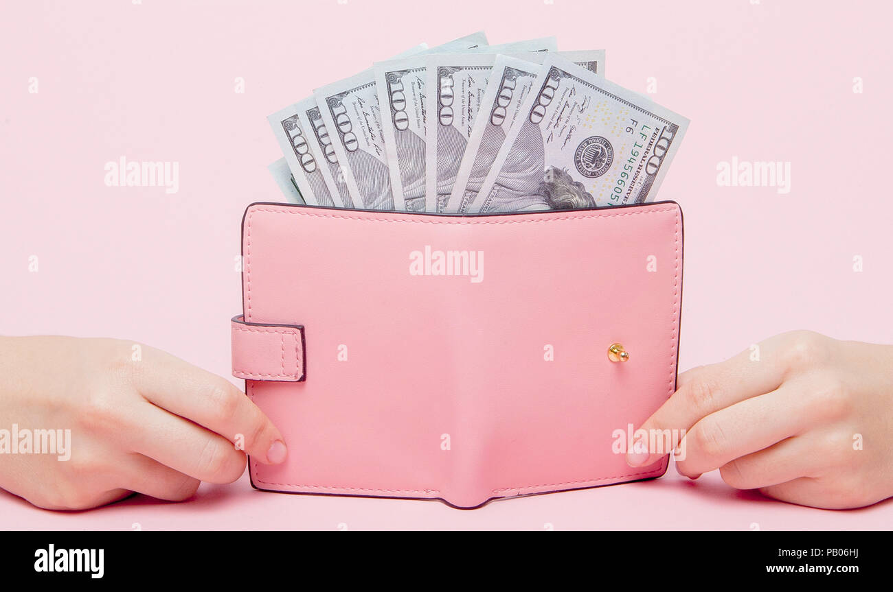 Dollars and pink wallet in woman's hand on a pink background with copy ...
