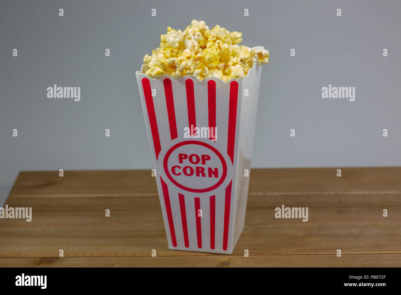 A red stripped popcorn small bucket overflowing with popcorn on a white ...