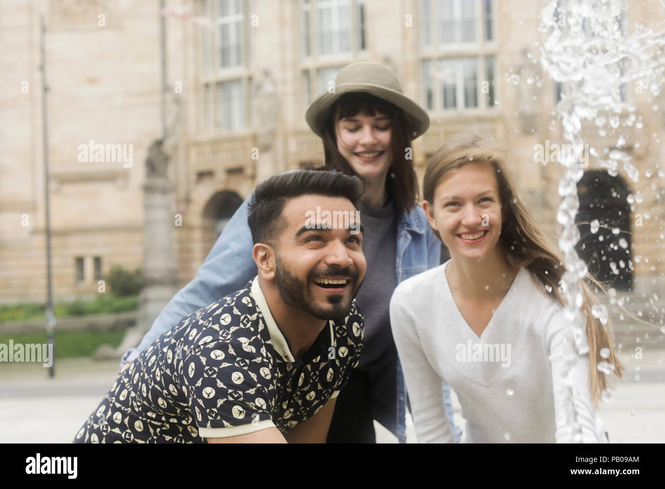 Three friends in the city playing with the water in a water fountain ...
