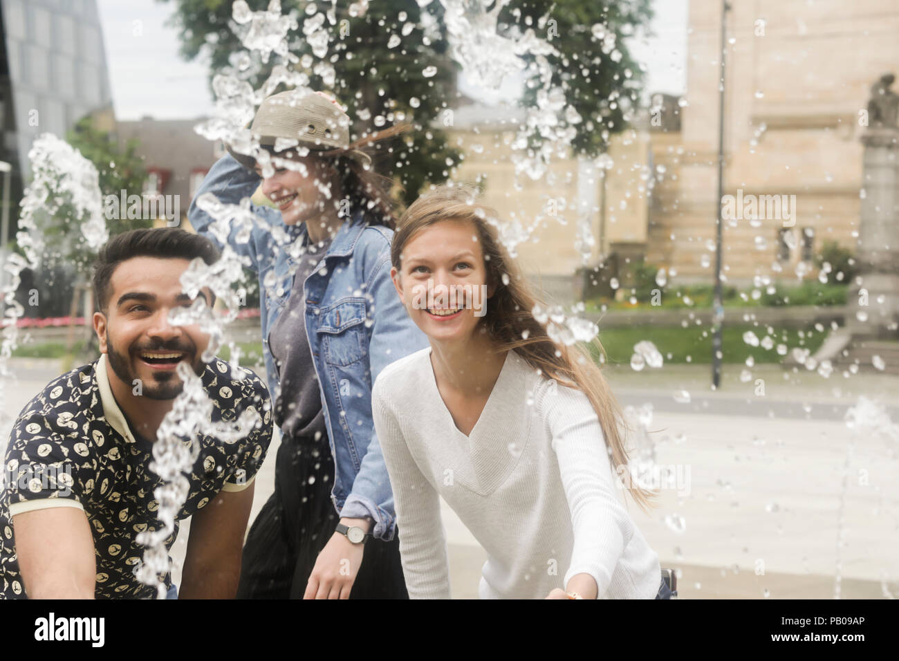 Three friends in the city playing with the water in a water fountain ...