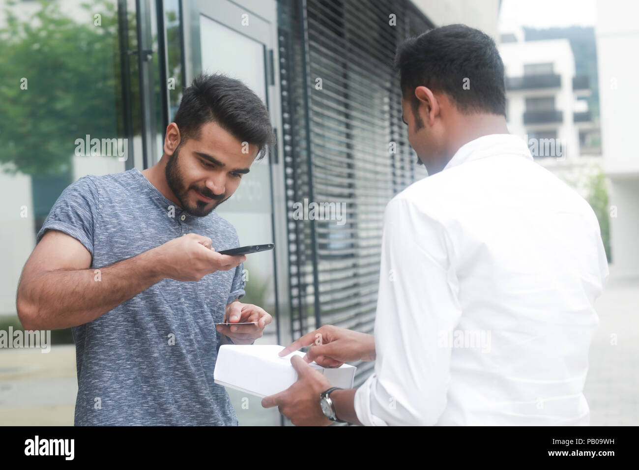 Two men standing outdoors photographing a parcel Stock Photo - Alamy