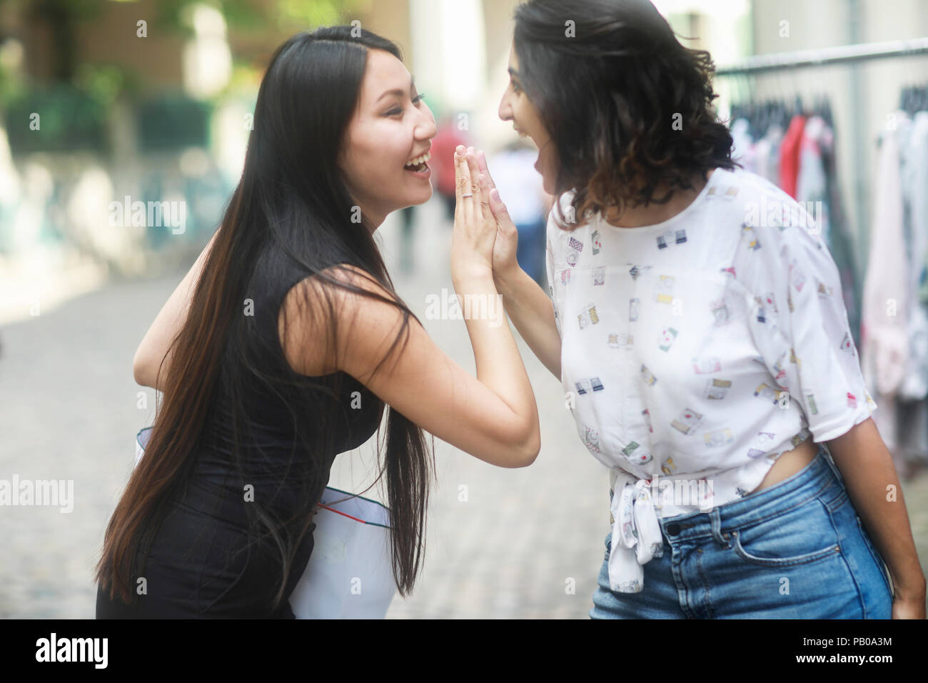 Two women standing in street high fiving Stock Photo - Alamy